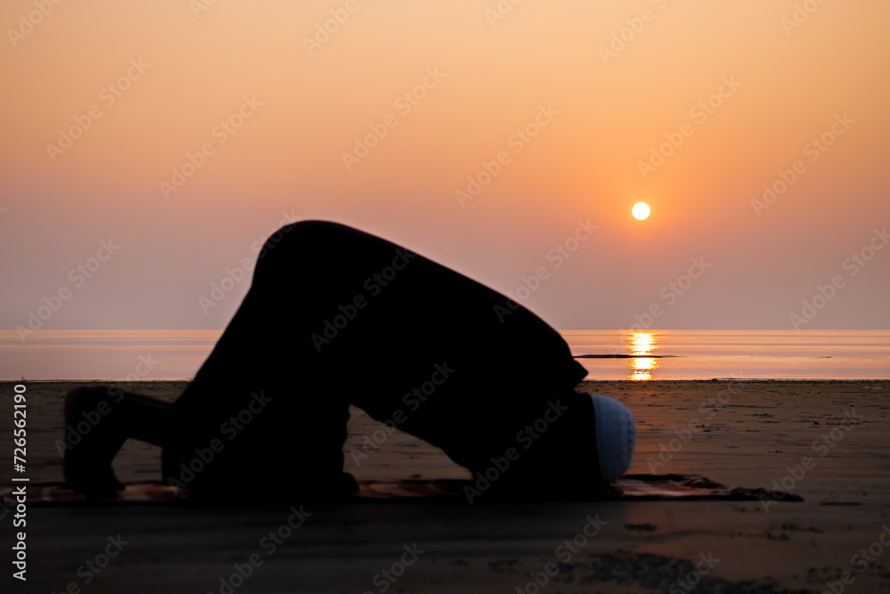 Asian Muslim man praying under the open sky by the sea at sunset ...