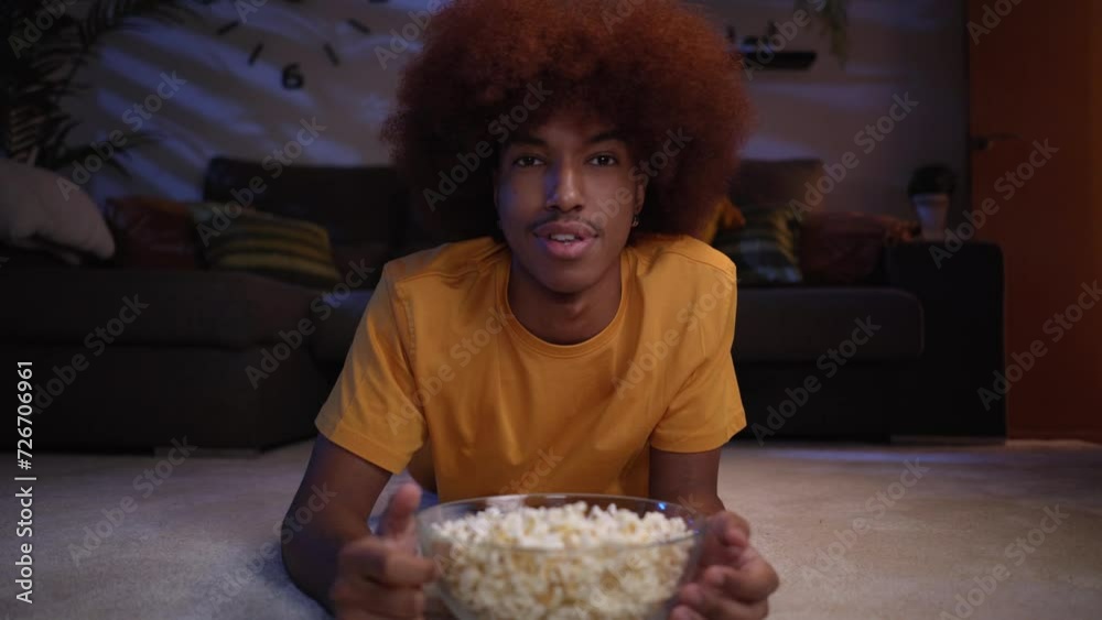 Point of view of a young African man watching movies at home eating popcorns and lying on the ...