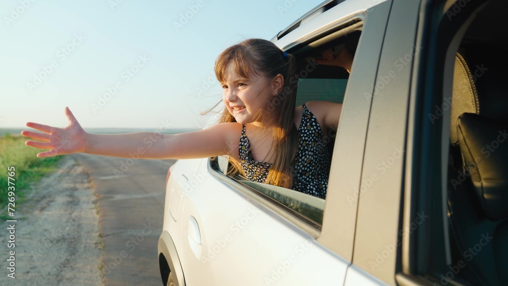 child girl face looks smiling from car out window, catching wind with ...