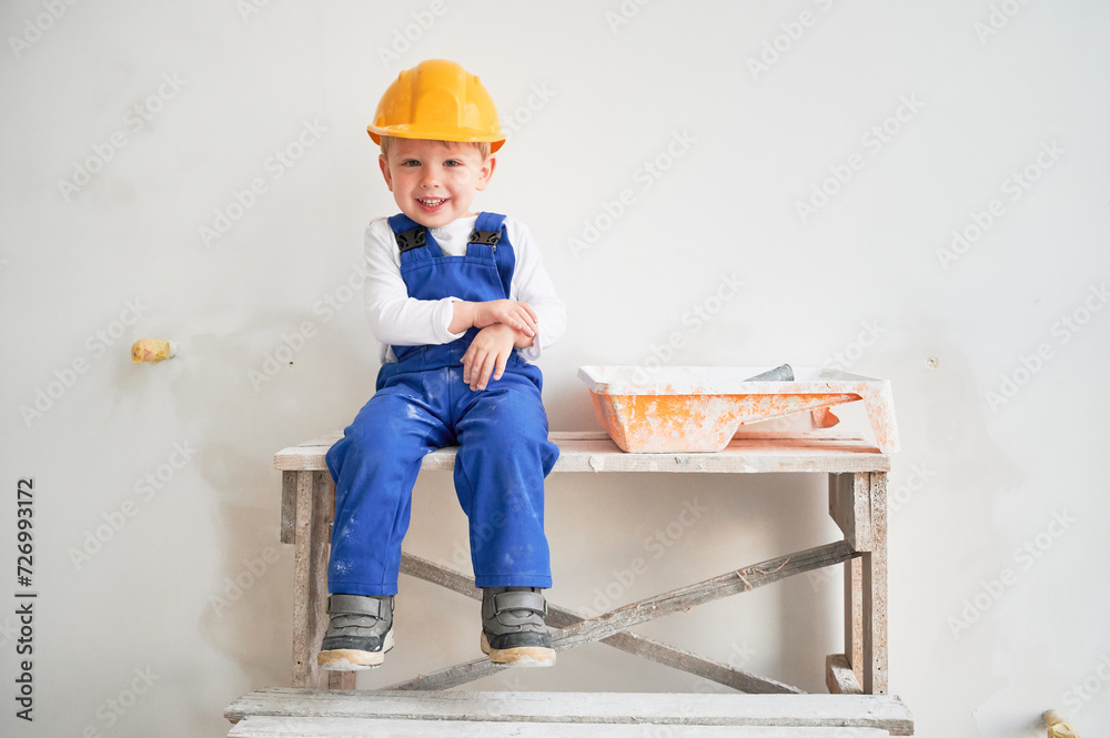 Cute kid construction worker sitting on wooden table against white wall ...