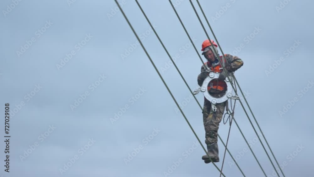 An aerial worker installs a separator for high-voltage wires while ...