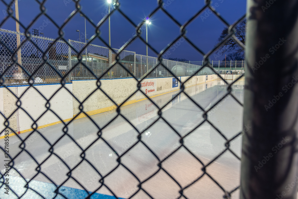 looking through a chain link fence to a recently resurfaced hockey rink ...