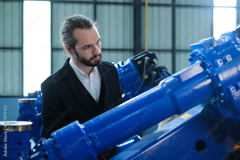 Bearded male engineer checking part number of automatic welding robotic ...