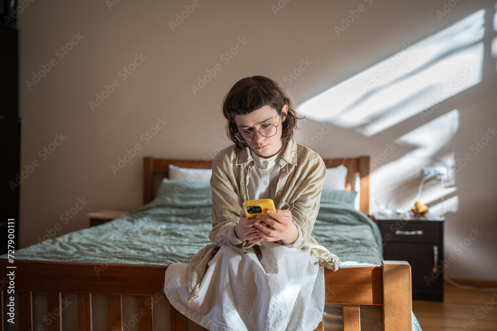 Sad lonely unhappy teenager sitting on bed, scrolling information ...