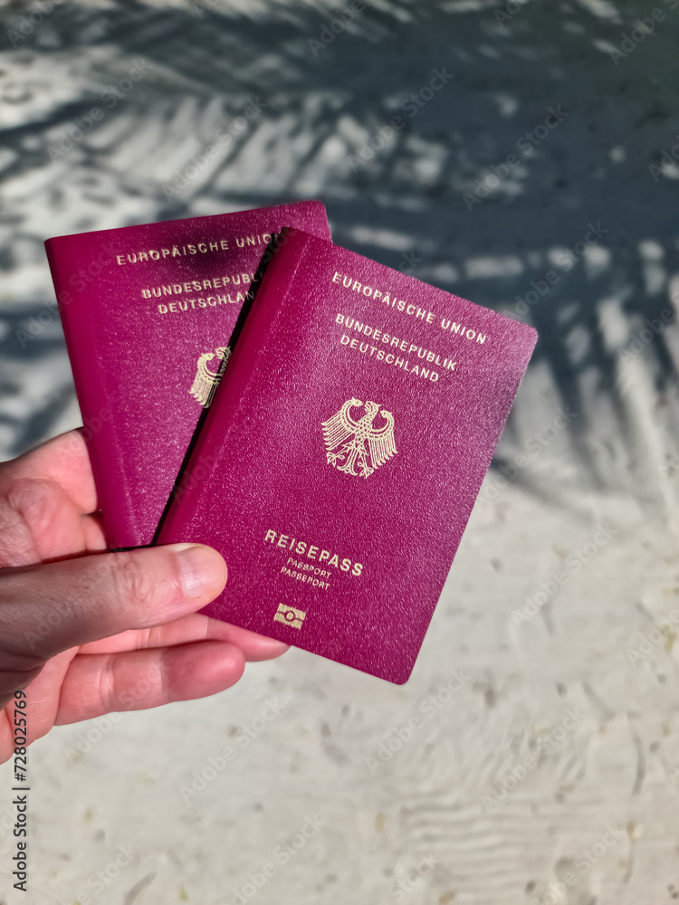 A hand holds two German passports in front of a soft travel background ...