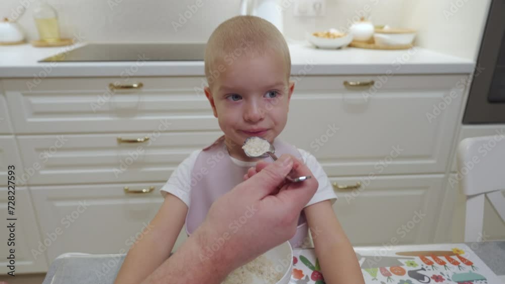 Father feeding his son oatmeal in the kitchen. 3-year-old child little ...