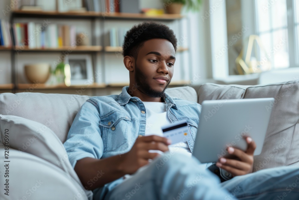 Young multiracial man sitting on the sofa holding a credit card with ...
