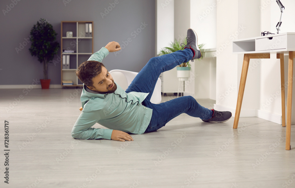 Young man fell off his chair in the office. Upset male employee wearing ...