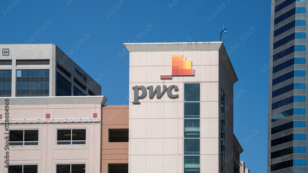 PwC company logo on a modern office building facade under a clear blue ...