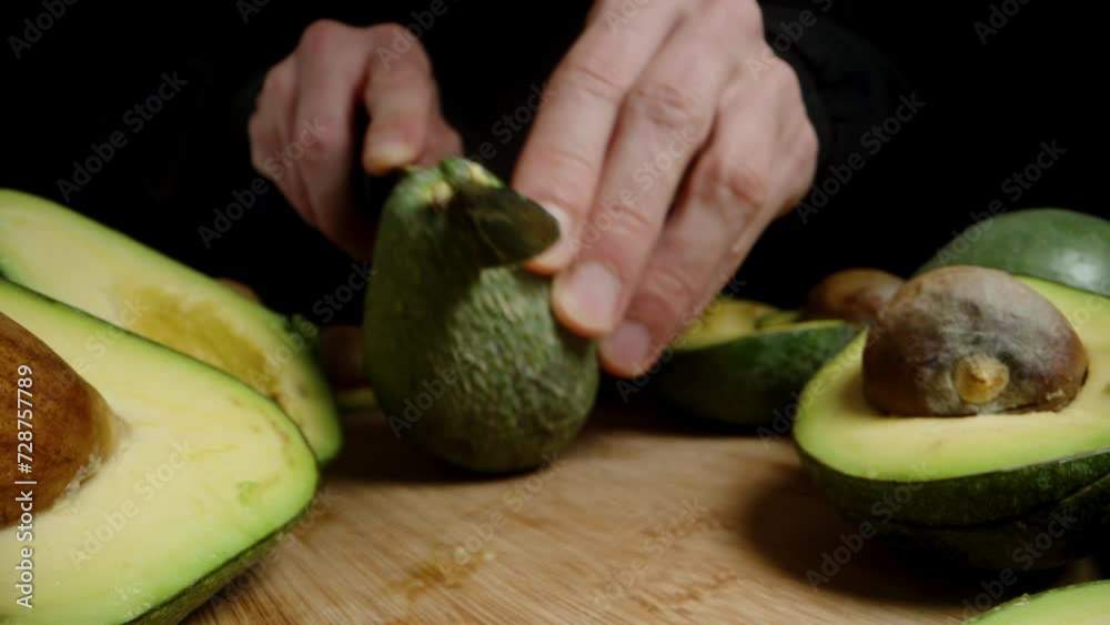 Vidéo Stock Against a black background, a man cuts open an avocado and ...