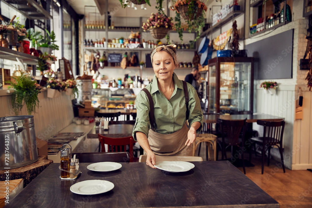 Middle aged waitress setting up plates on restaurant table Stock Photo ...