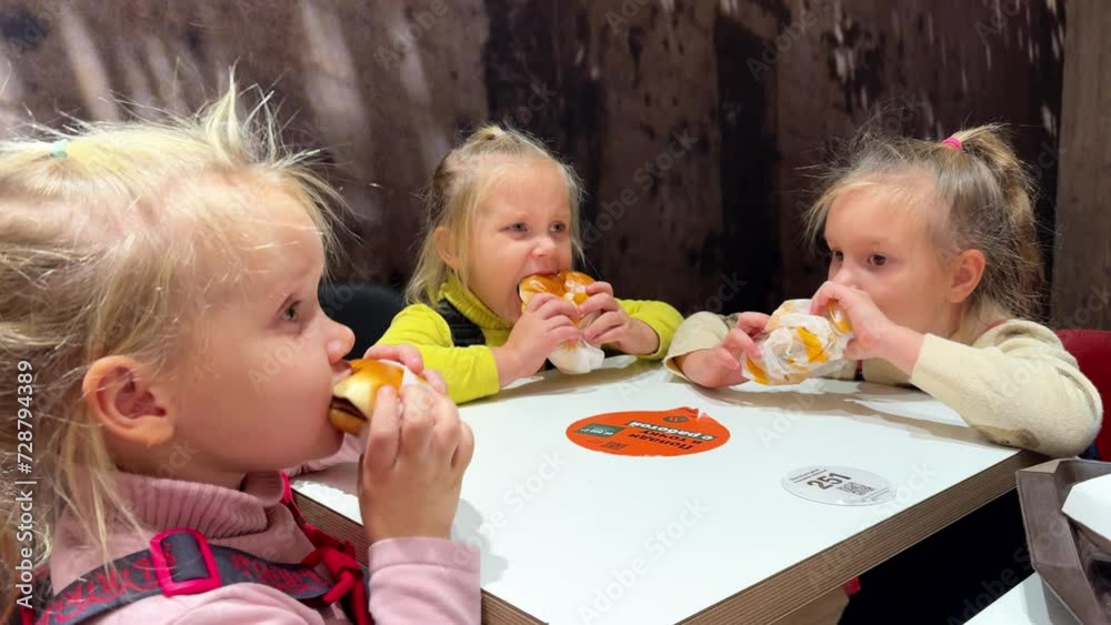 Twins triplets sisters eating burgers with their hands sitting in a ...