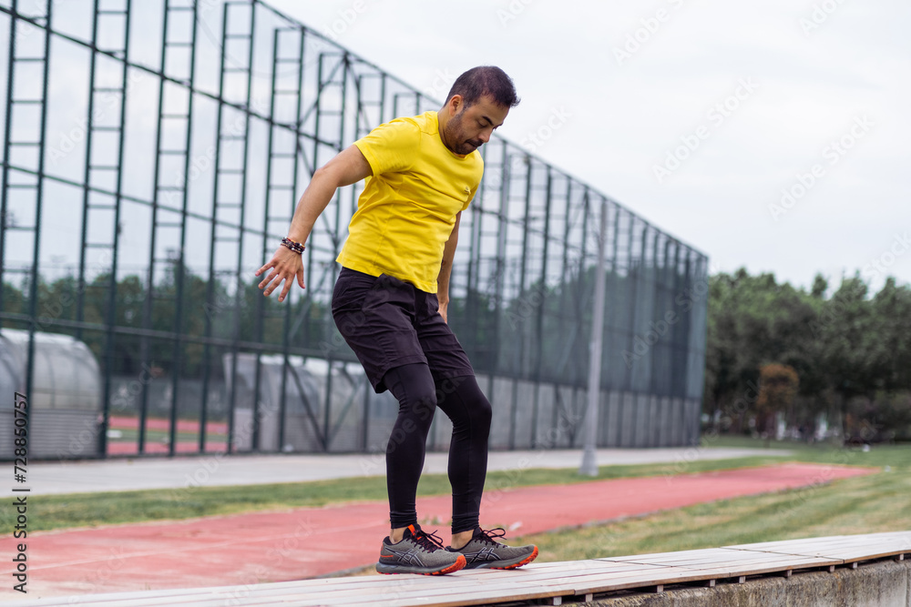 Sportsman in tracksuit jumping on bench near large open stadium in ...