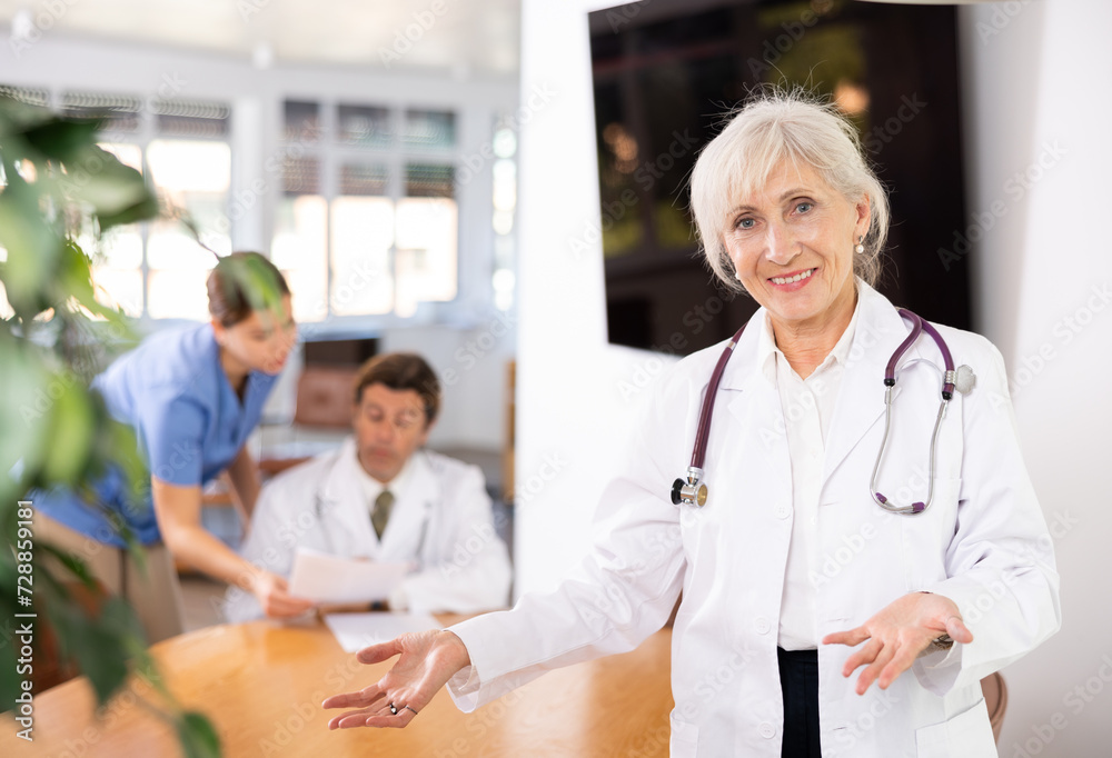 Smiling friendly elderly female doctor in white coat making welcome ...