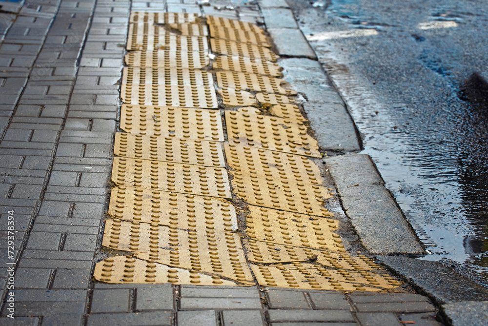 Dented yellow tactile tiles on sidewalk in front of pedestrian crossing ...