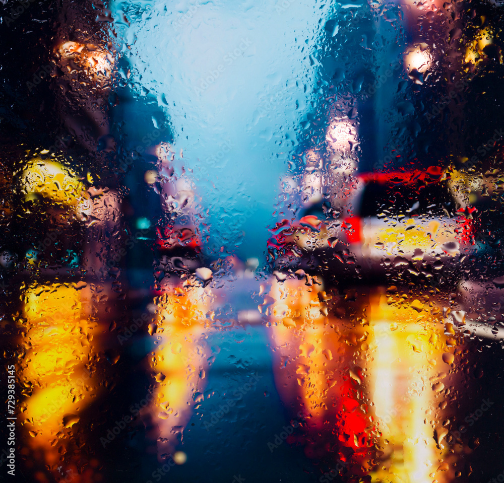 View through a glass window with raindrops on city streets with cars in ...