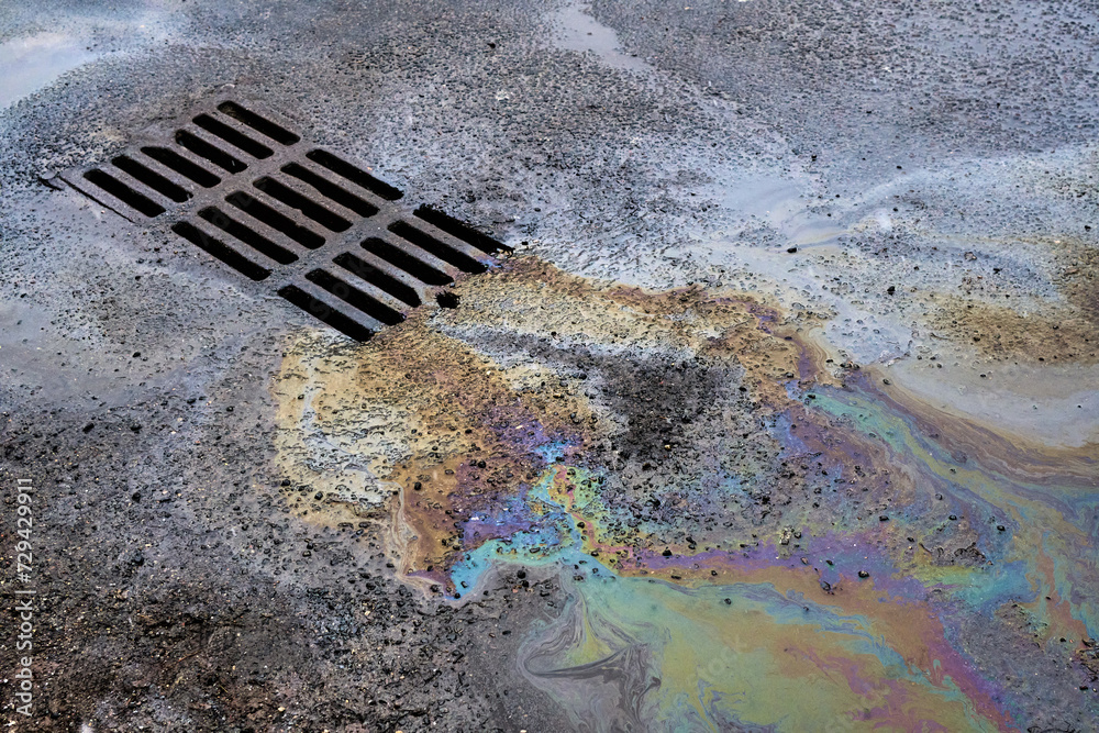 An oil or gasoline slick against the backdrop of an asphalt road flows ...