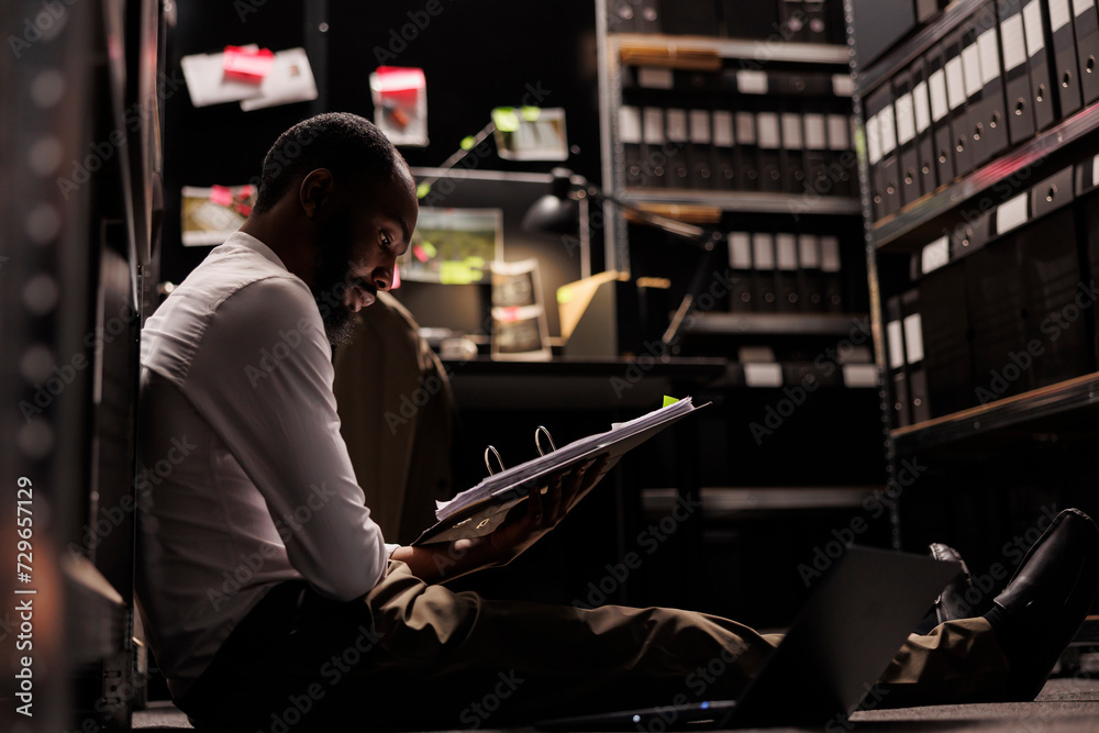 African american policeman reading crime case folder on floor in dark ...