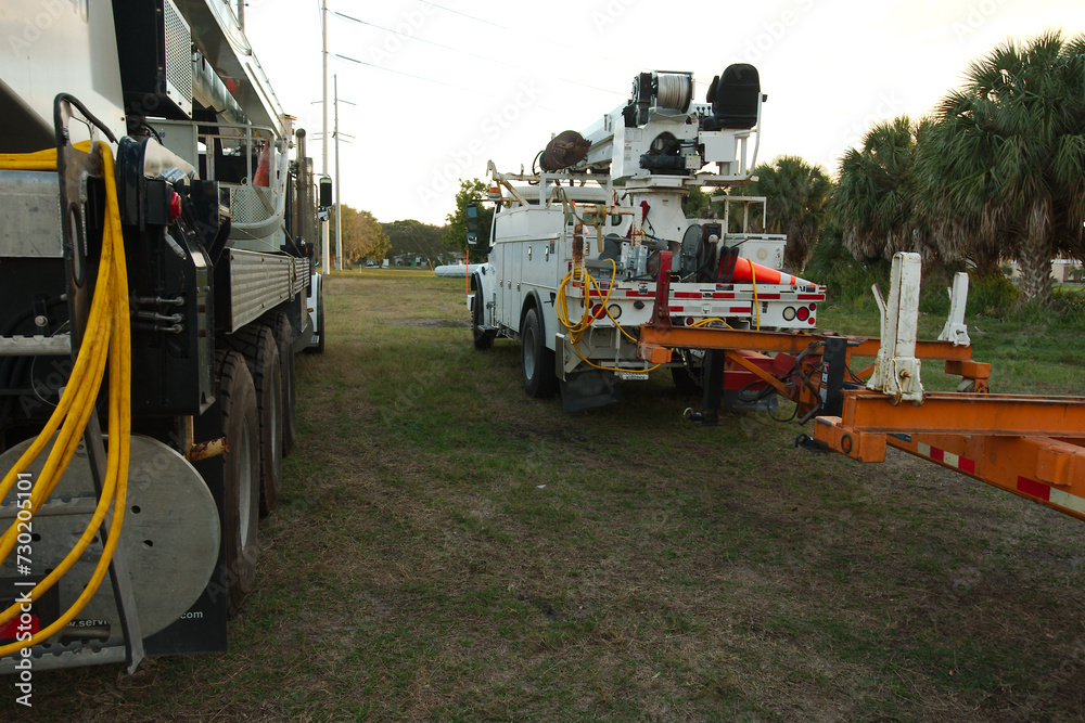Rear view of two electric utility trucks in grass field with overhead ...