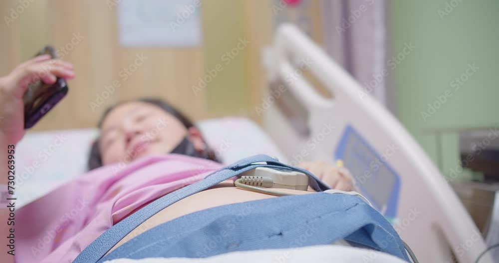 Pregnant woman lying in a hospital bed, fetal monitor strapped to her ...