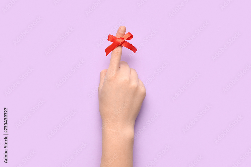 Female hand with red bow on index finger against lilac background ...