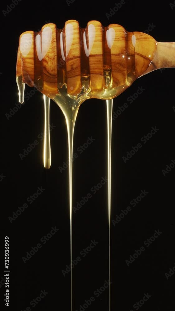 Drops of honey flow from a wooden honey dipper and slowly drip down ...