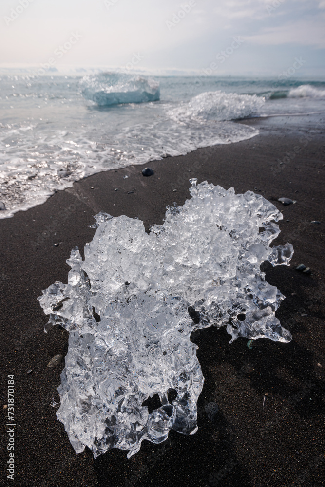 Ocean waves lapping up chunks of ice sparkling in the sun on a black ...