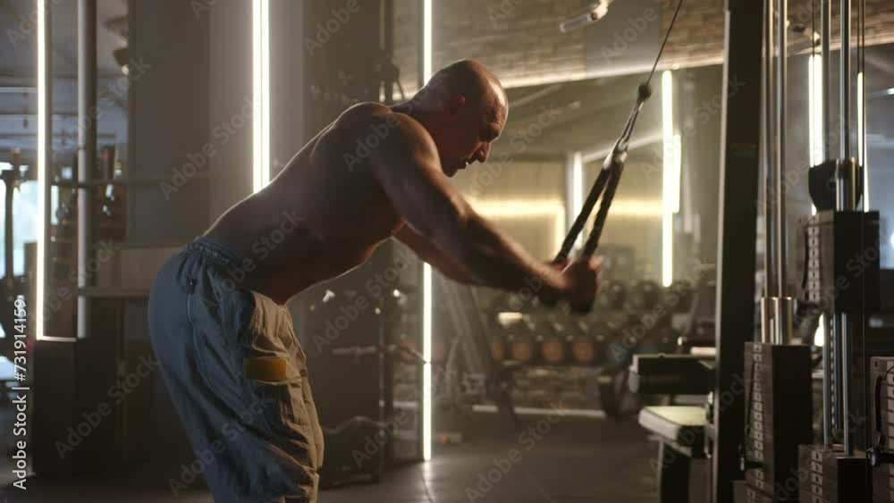 A bald man at the gym is fully concentrated on performing tricep ...