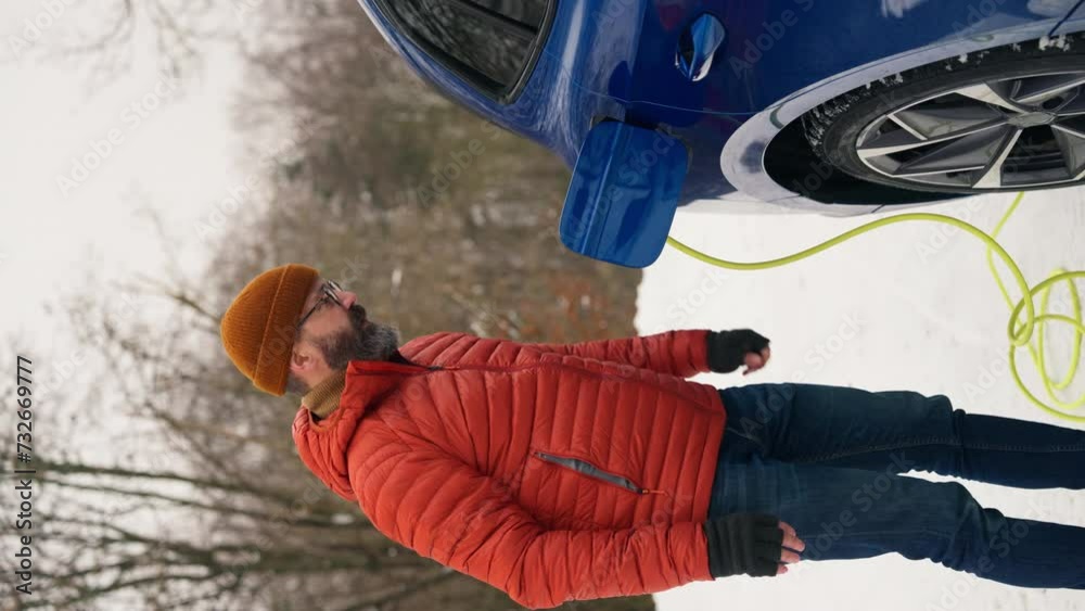 Man charging electric car during cold snowy day. Side view of hansome ...
