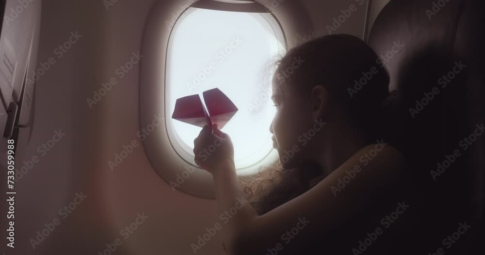 Child sitting by aircraft window and playing with little paper plane ...