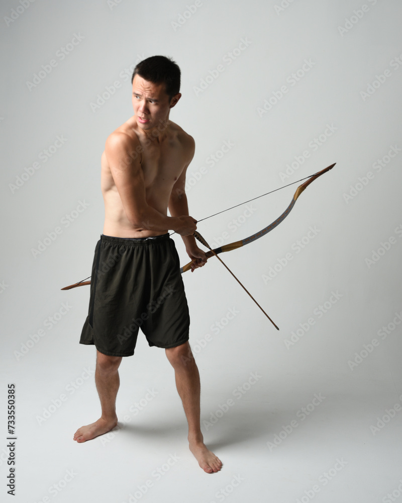 Full length portrait of fit asian male model, Holding hunting bow and ...
