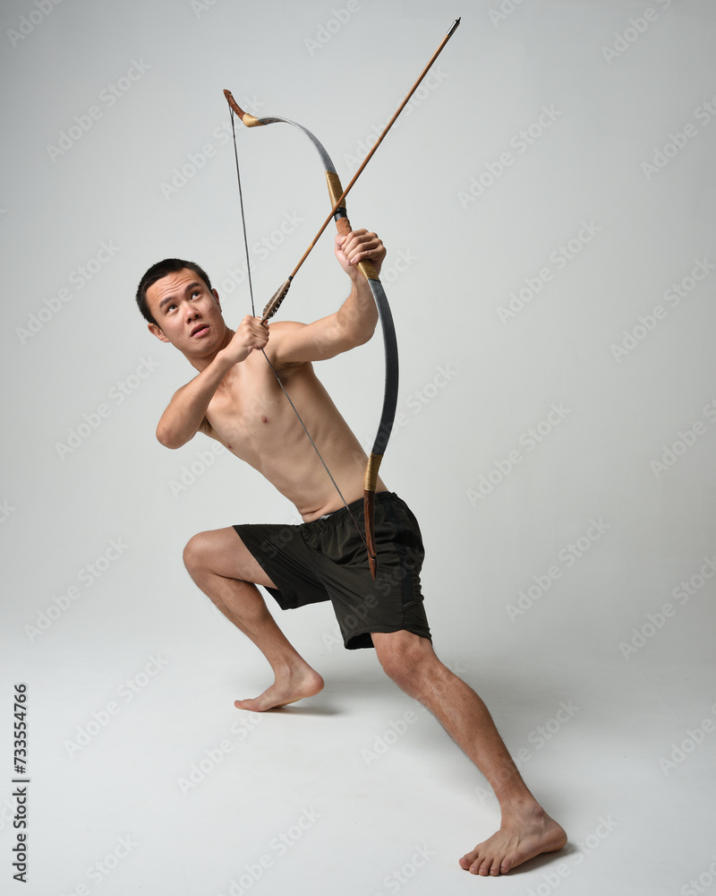 Full length portrait of fit asian male model, Holding hunting bow and ...