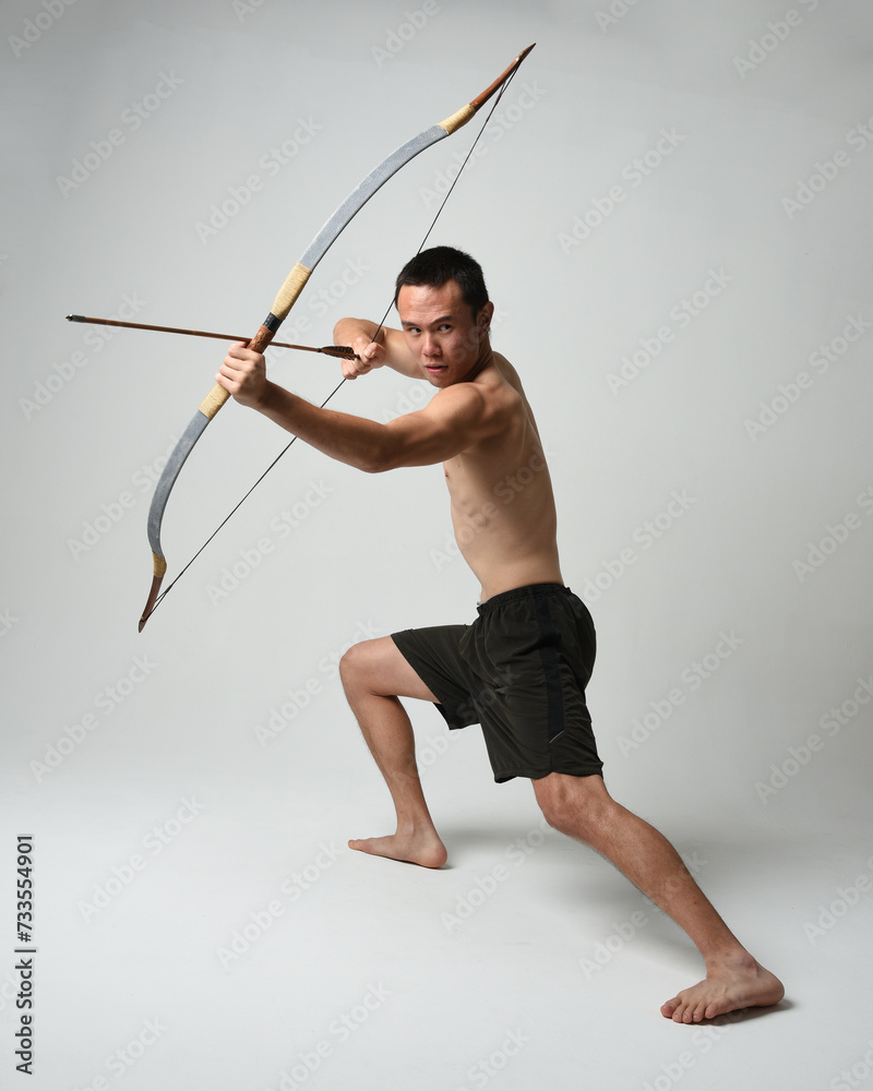 Full length portrait of fit asian male model, Holding hunting bow and ...