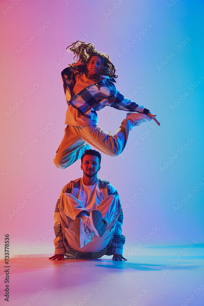 Dance duet. Woman jumps over man crouching in radiant neon glow ...