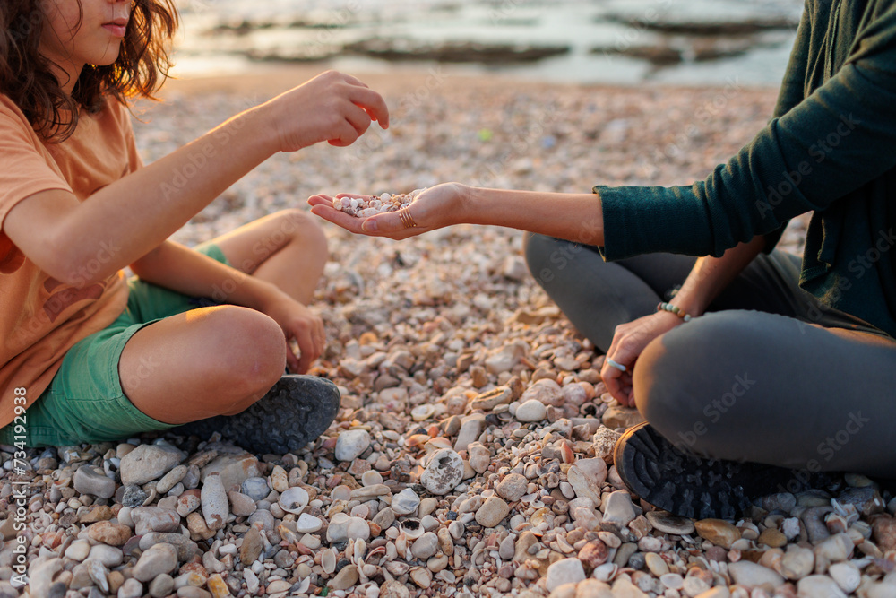 child collects shells and pebbles on a sandy beach with a caring, kind ...