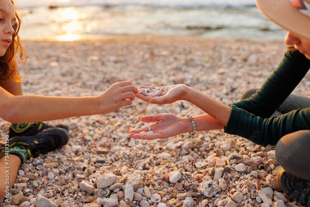child collects shells and pebbles on a sandy beach with a caring, kind ...