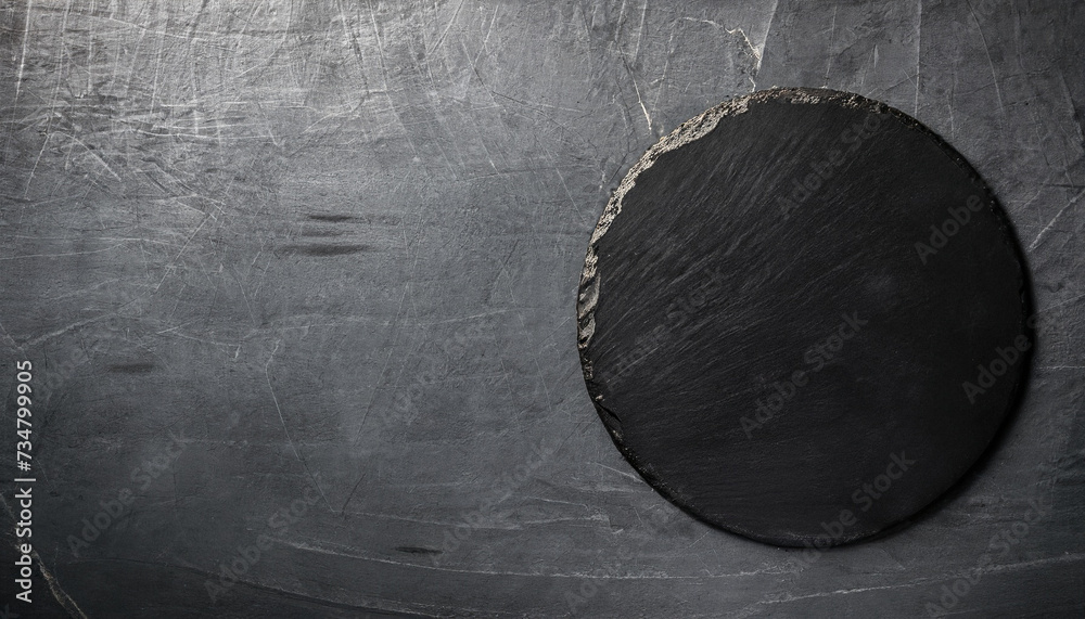 Round black slate stone plate in the middle of a dark grunge scratched ...