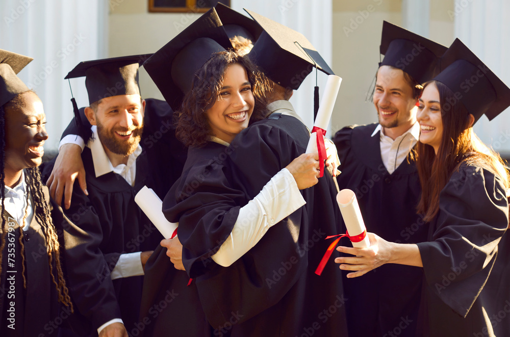 Happy smiling diverse group of students graduates hugging outdoors ...