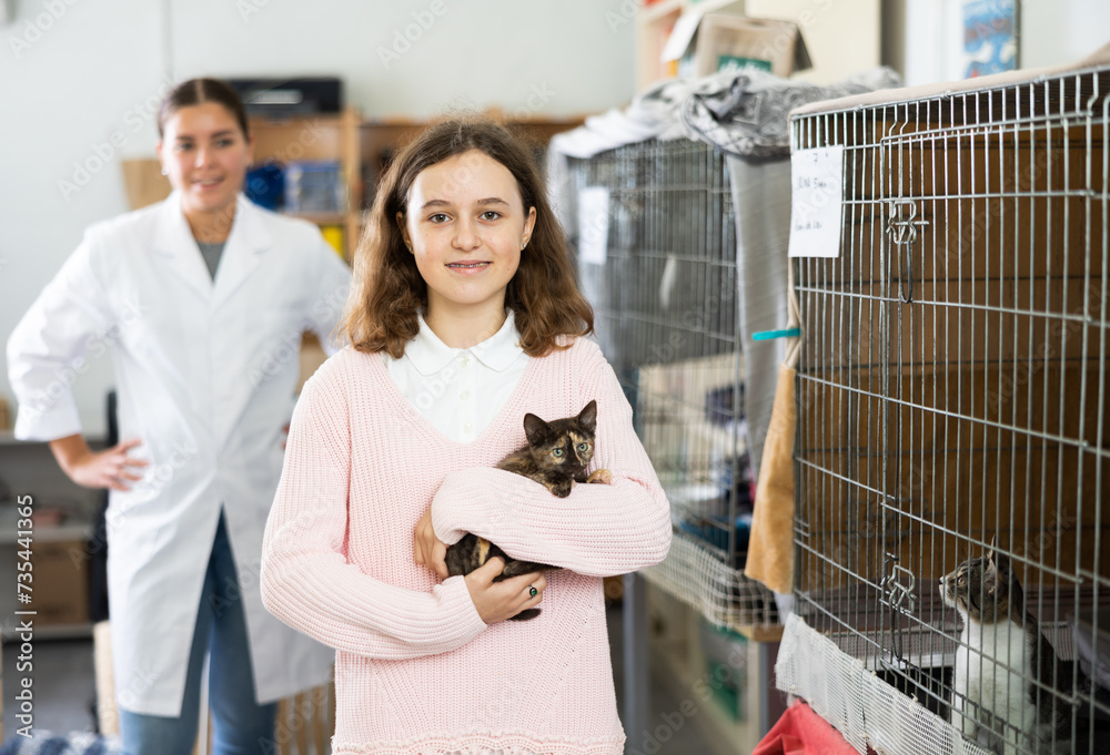 Smiling interested preteen girl holding cute mottled kitten in hands ...