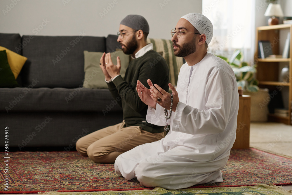 Two young Muslim men with open palms standing on knees on the carpet ...