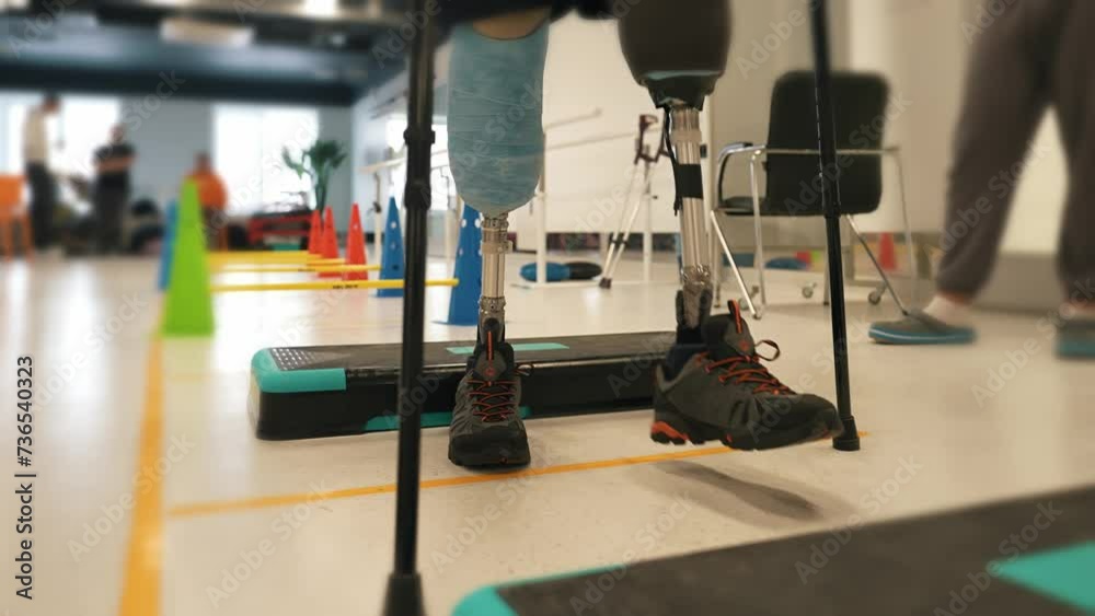 A disabled person with two prosthetic legs is undergoing rehabilitation ...
