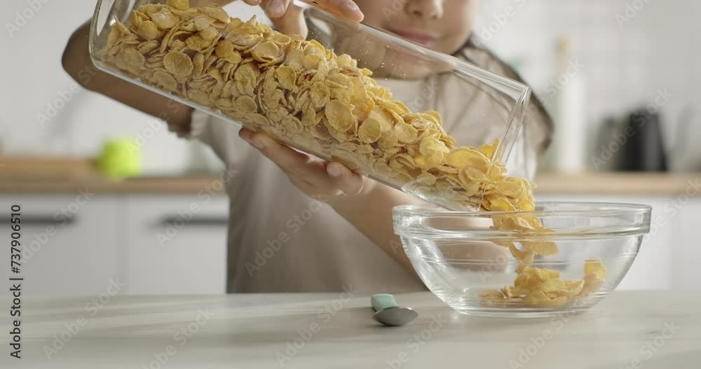 Close-up kid girl pours corn flakes into a bowl at breakfast. Little ...