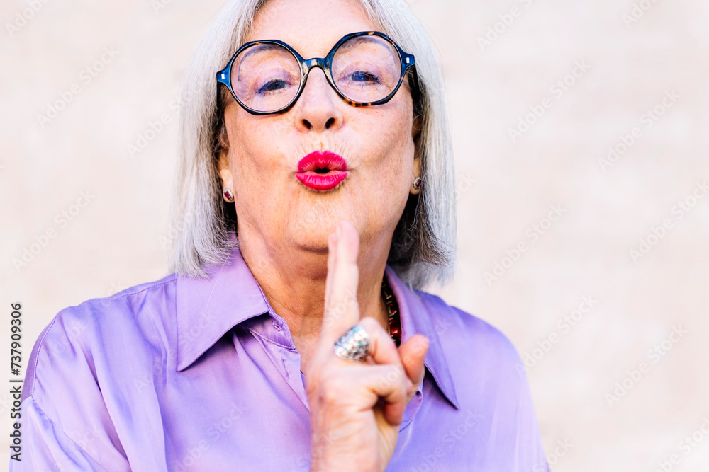 portrait of a nice senior woman blowing on her fingers like a gun after ...