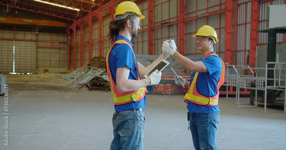 Two construction engineer workers in hard hats and vests engage in a ...