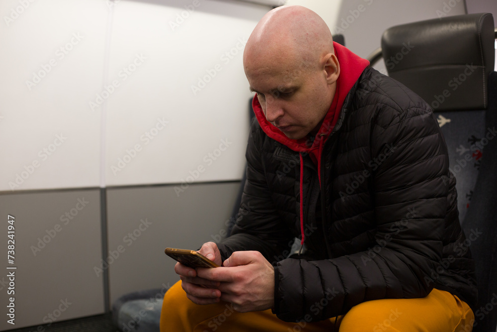 Bald white man sitting on train and playing on the phone during the ...