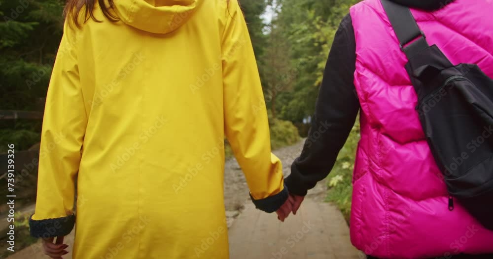Two people holding hands wearing colorful jackets on a forest trail ...