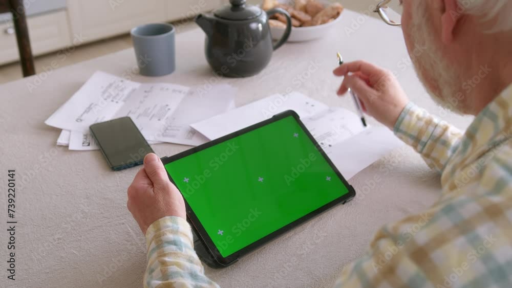 elderly grey haired man in glasses sitting and using tablet with green ...
