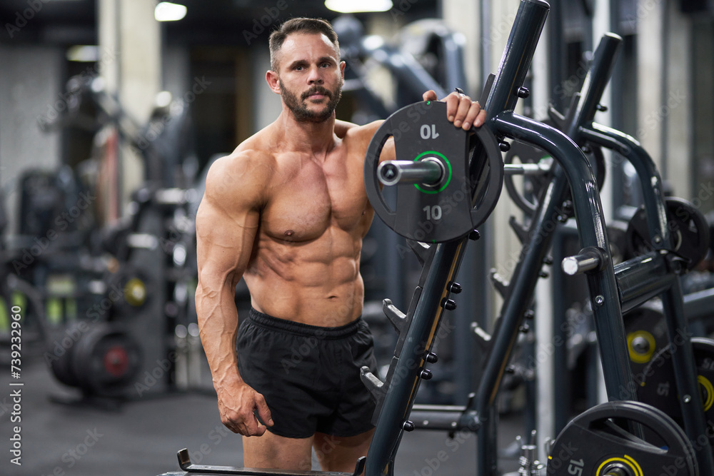 Handsome sportsman posing, while leaning on training apparatus in gym ...