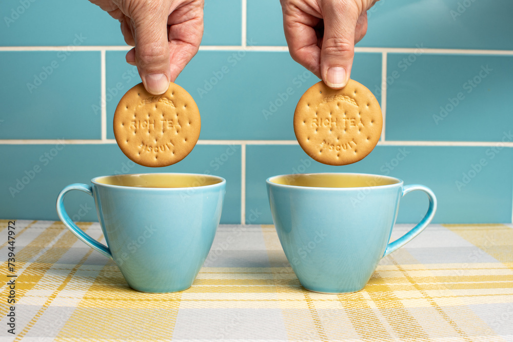 Cups of tea in attractive blue and yellow cups with hands dunking rich ...
