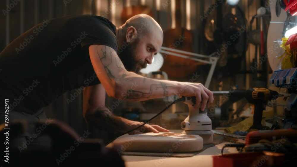 Professional male craftsman grinds wooden guitar body on table using ...